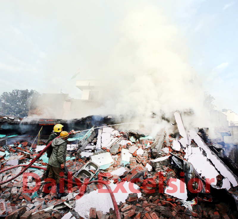 Fire fighters dousing flames coming out from the debris of a building ...